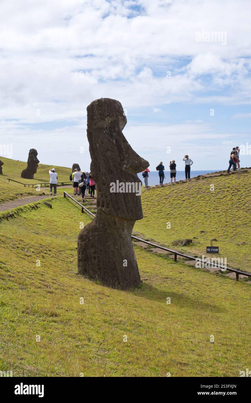 Tourists walk by half buried Moai (monolithic statues) at Rano Raraku ...