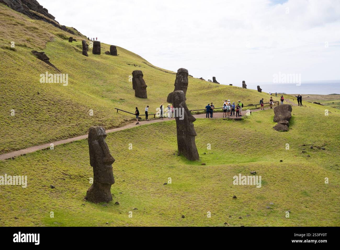 Tourists walk by half buried Moai (monolithic statues) at Rano Raraku ...