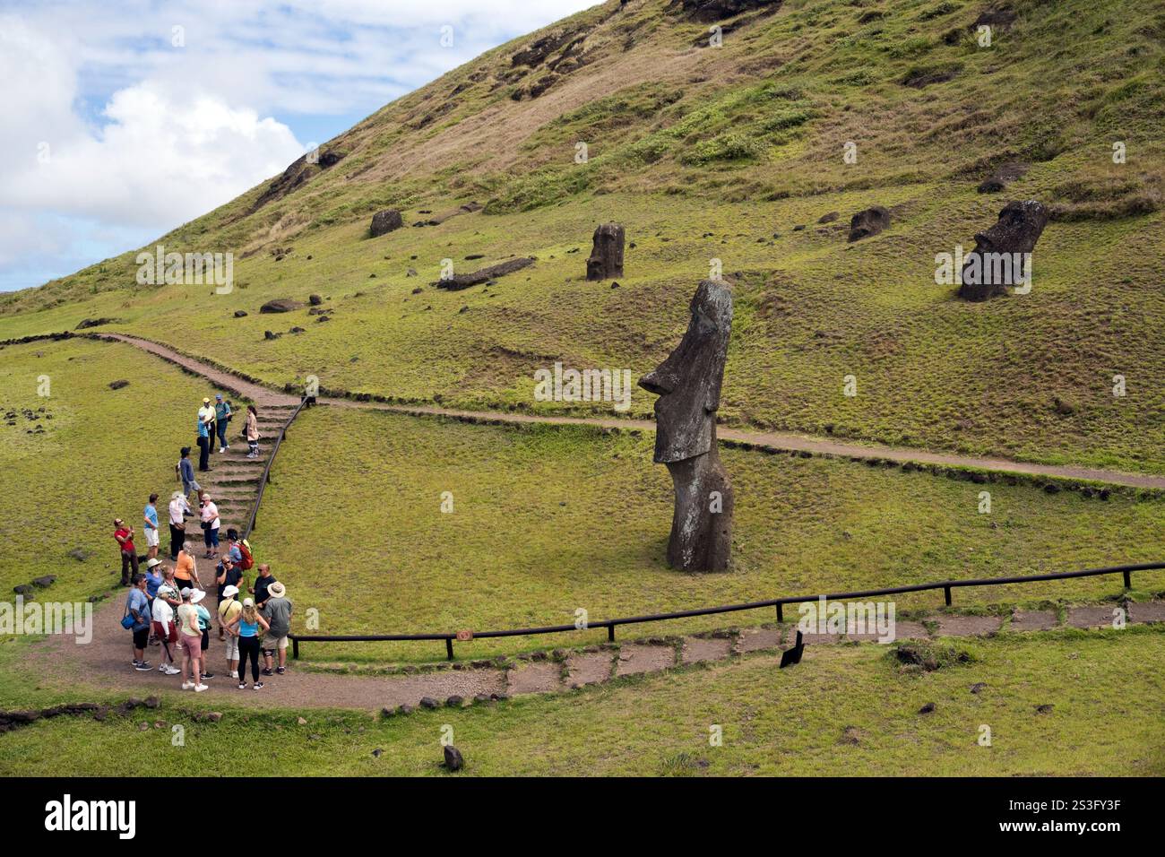 Tourists walk by half buried Moai (monolithic statues) at Rano Raraku ...