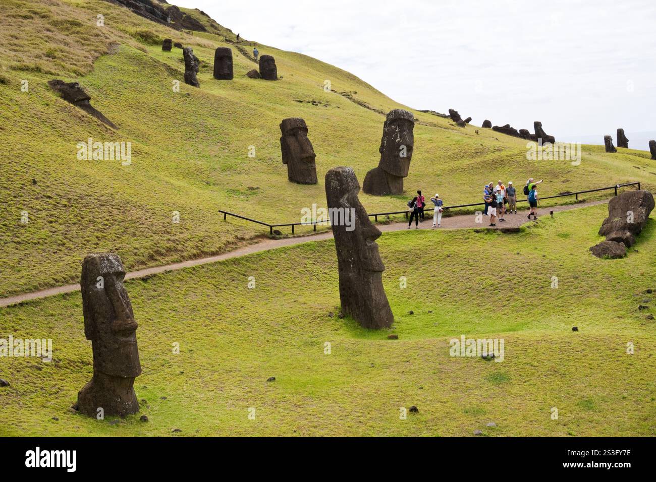 Tourists walk by half buried Moai (monolithic statues) at Rano Raraku ...