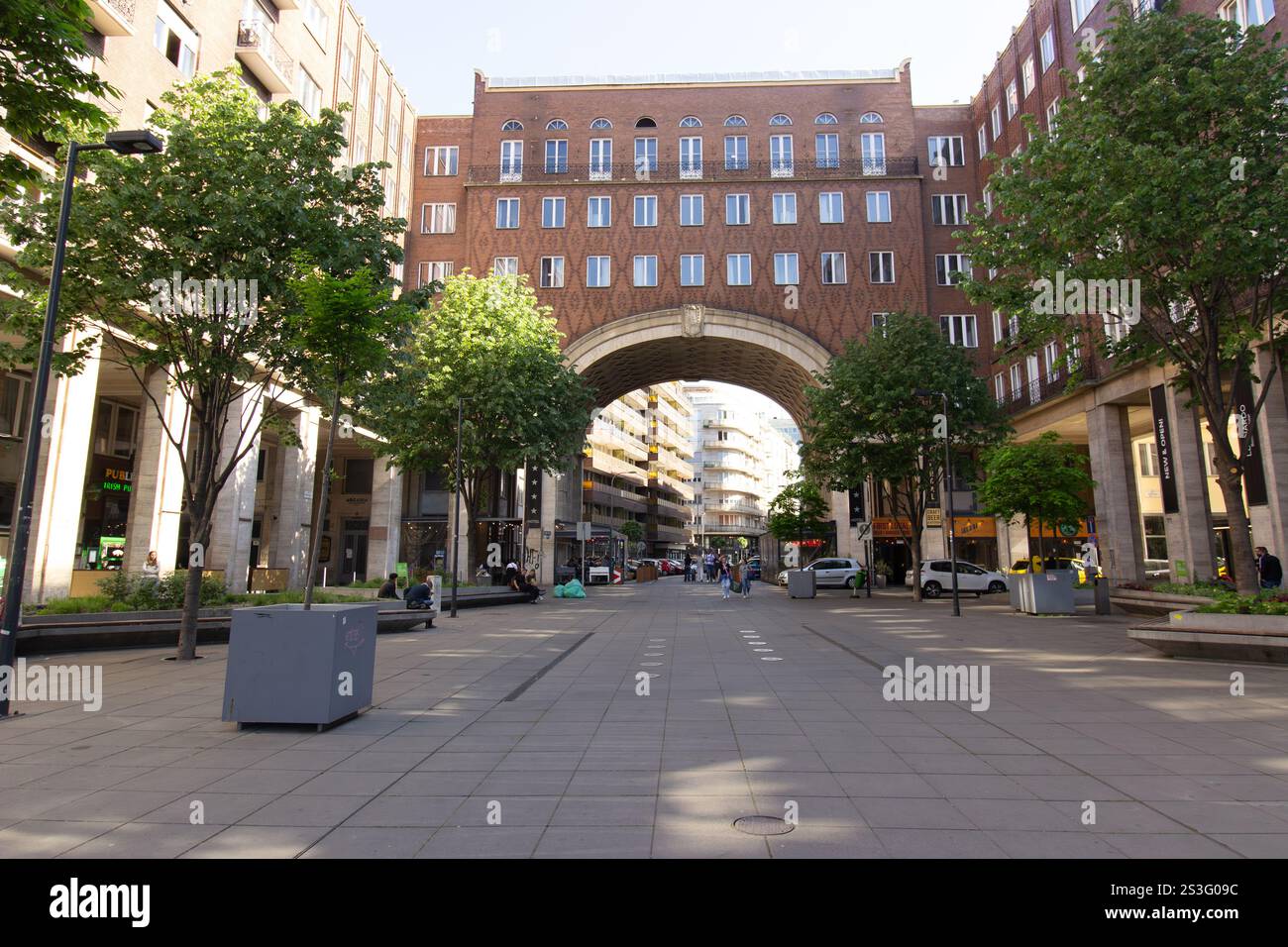 Wide pedestrian street with modern buildings, trees, and an arched ...