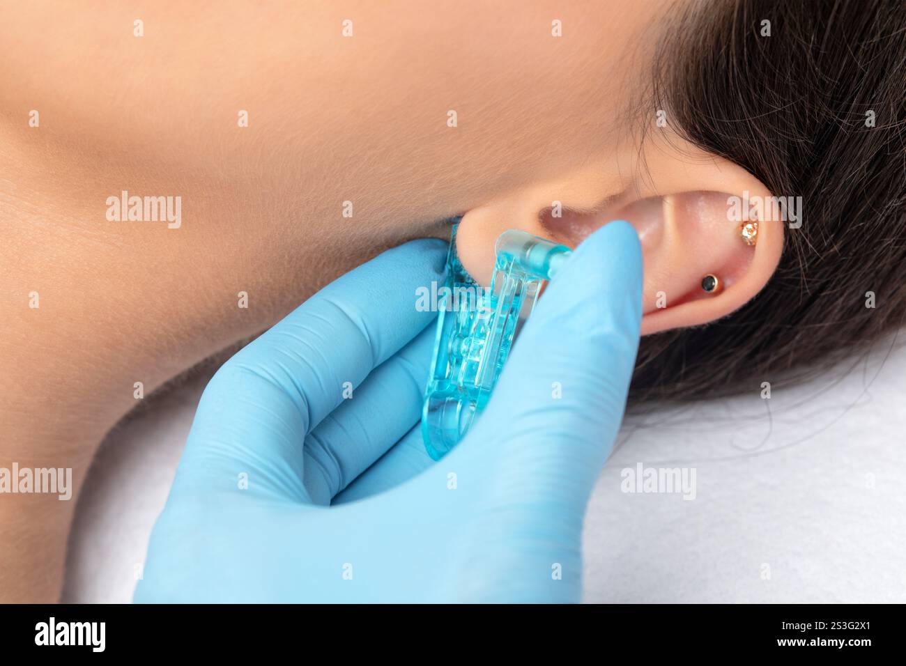 A beautician makes a puncture of the earlobe with a disposable device ...