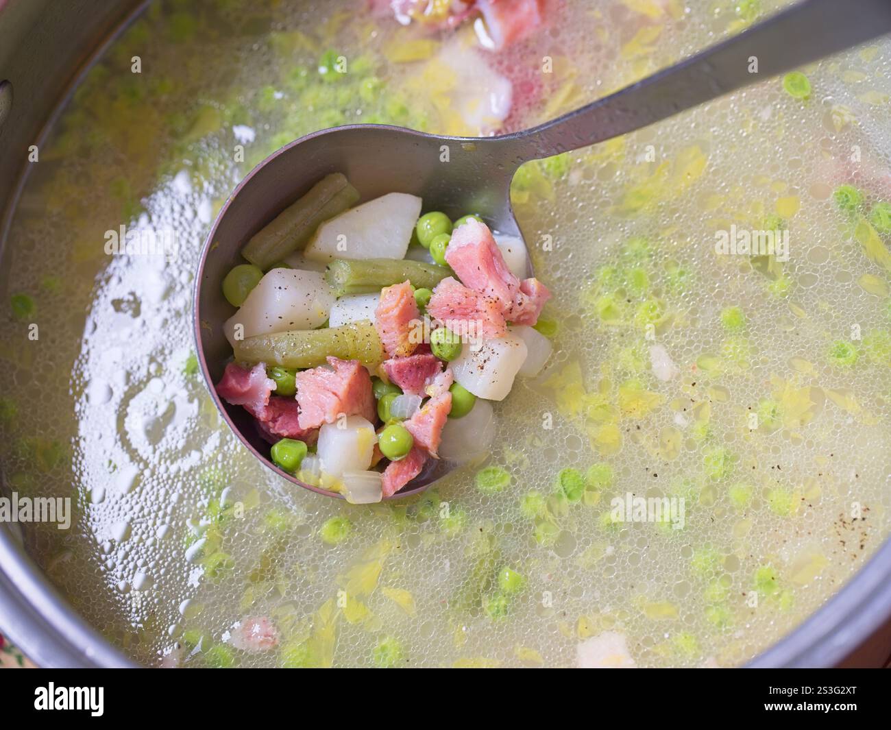 Scooping out a ladle full of ham, potato, and pea soup from the pot ...