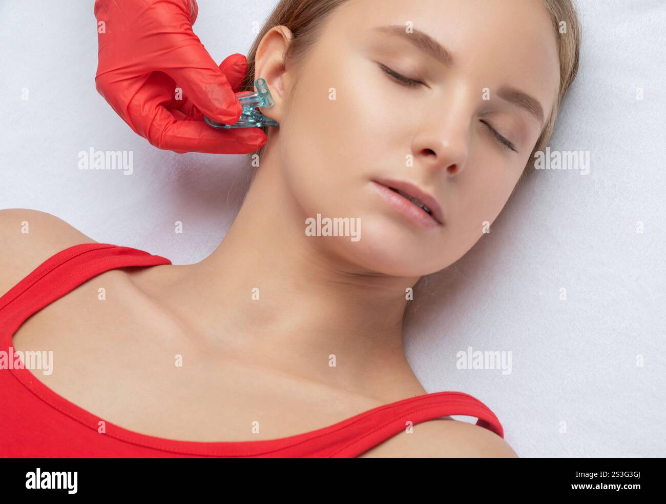 A beautician makes a puncture of the earlobe with a disposable device ...