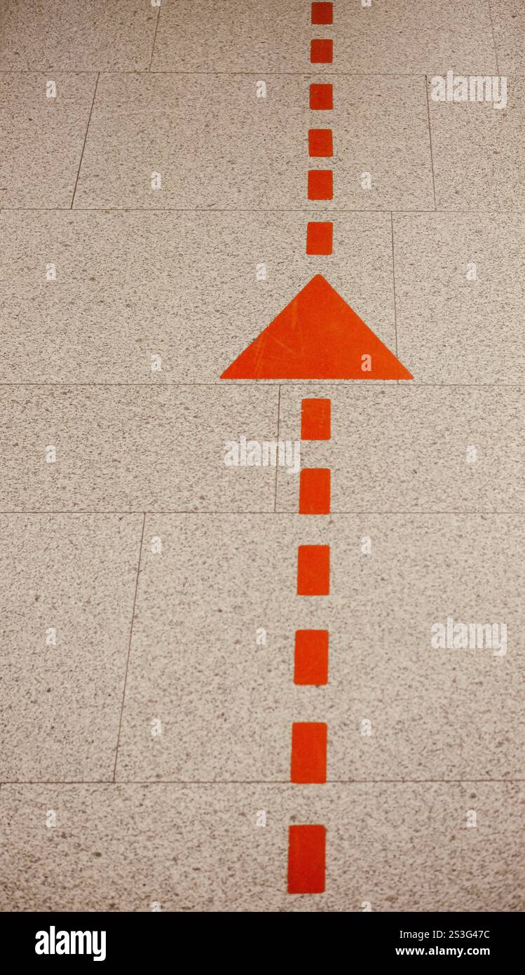 An overhead shot depicts a beige tiled floor with an orange upward ...