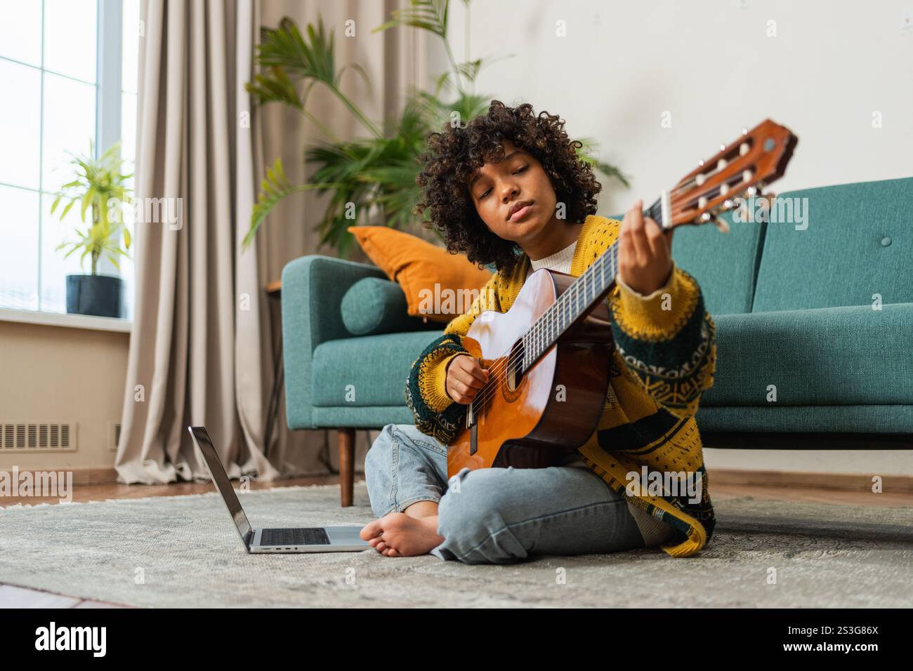 African American woman learning guitar watching tutorial on laptop at ...
