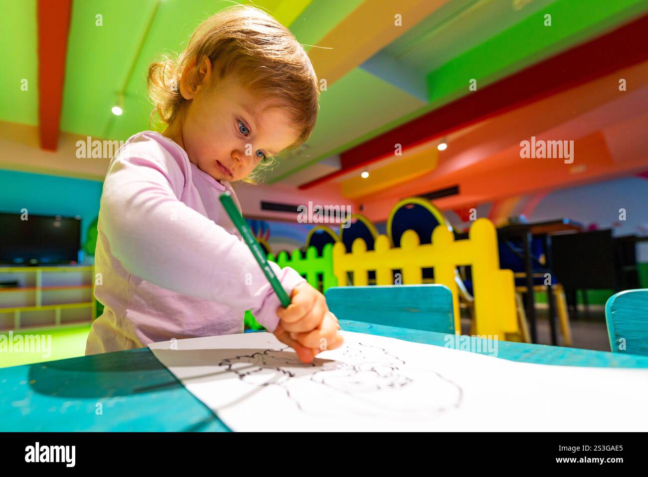 A creative child drawing with a pencil in a colorful indoor play area ...