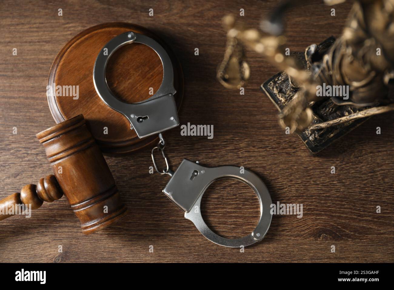 Handcuffs, judge's gavel and Lady Justice figure on wooden table, flat ...