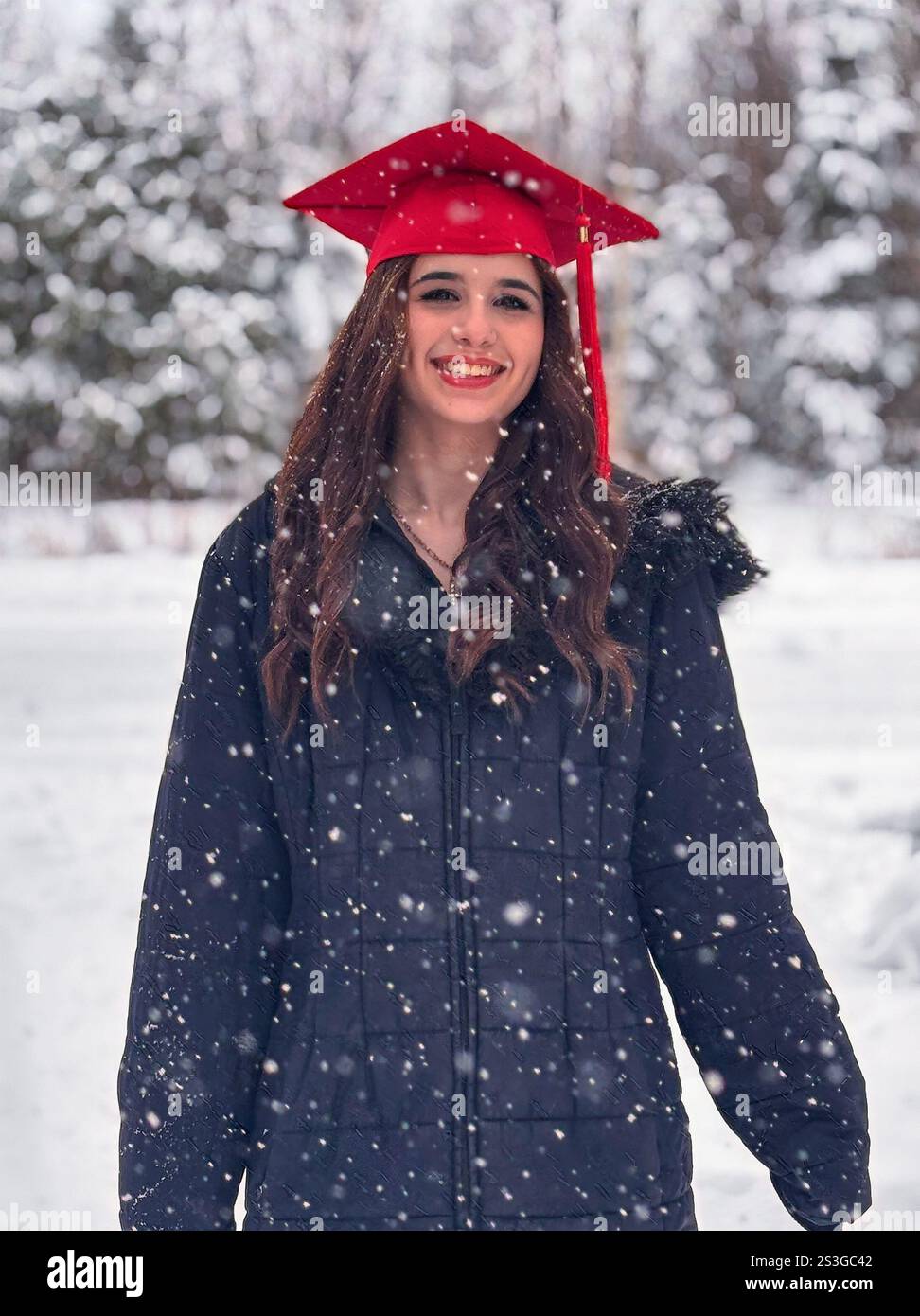Graduating girl with long brunette hair wearing red cap, and winter ...