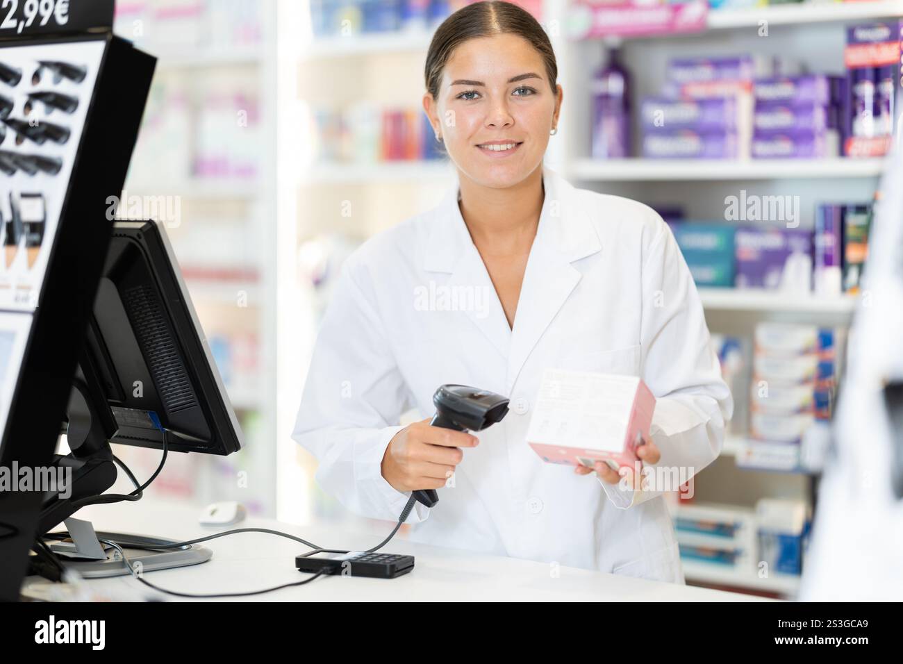 Girl pharmacist in cash area works with computer and goods, scans drugs ...