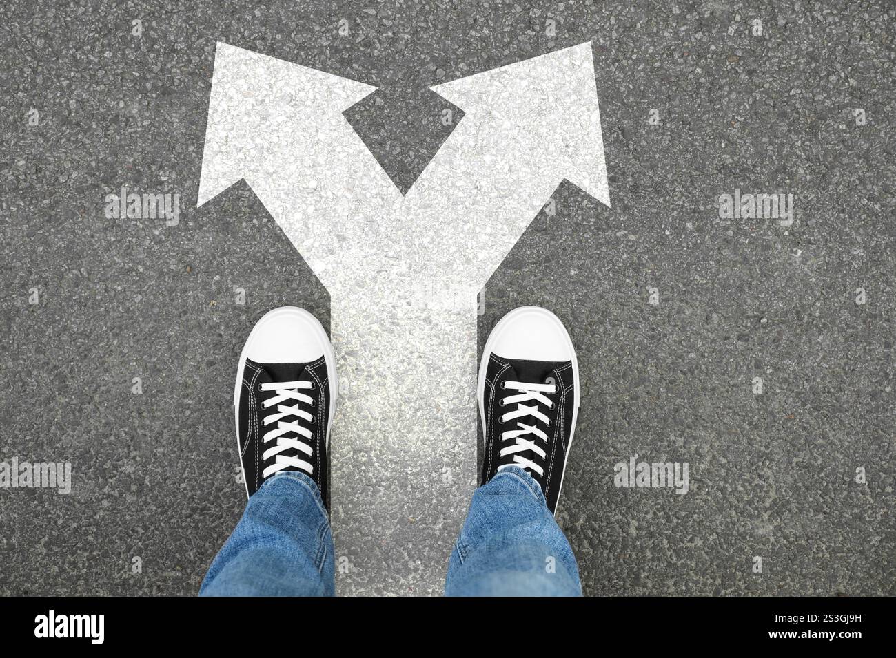 Man standing on asphalt road with white arrows pointing in different ...