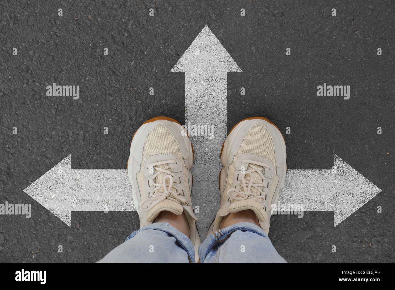 Woman standing on asphalt road with white arrows pointing in different ...