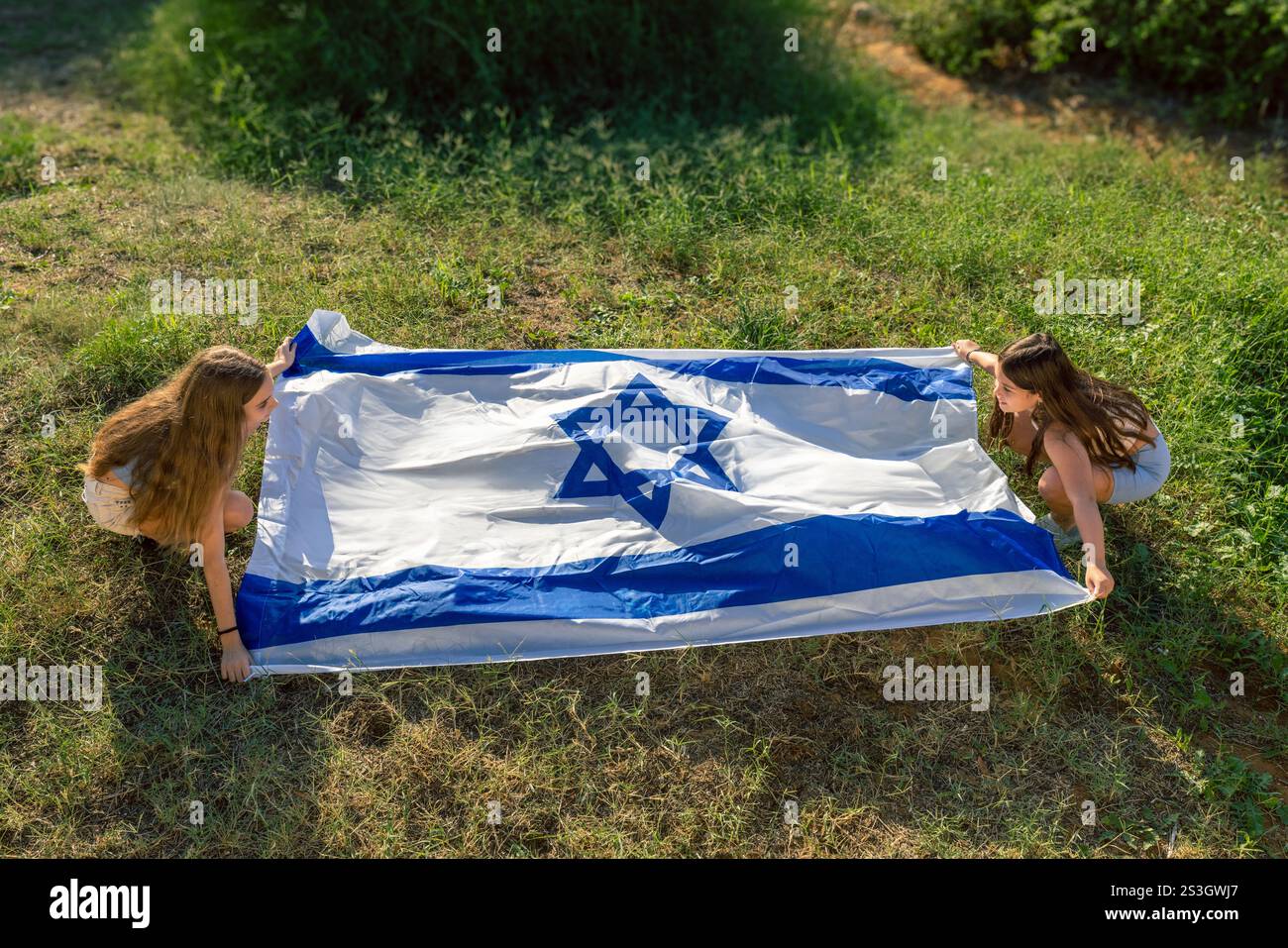 Two girls spread the flag of Israel as a tablecloth on the grass for a ...