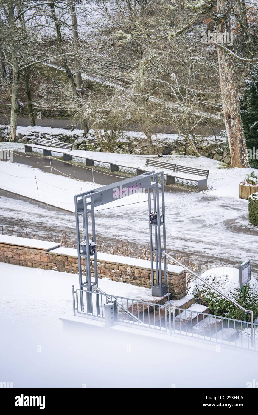 A quiet park in winter with snow-covered paths, trees and an empty ...
