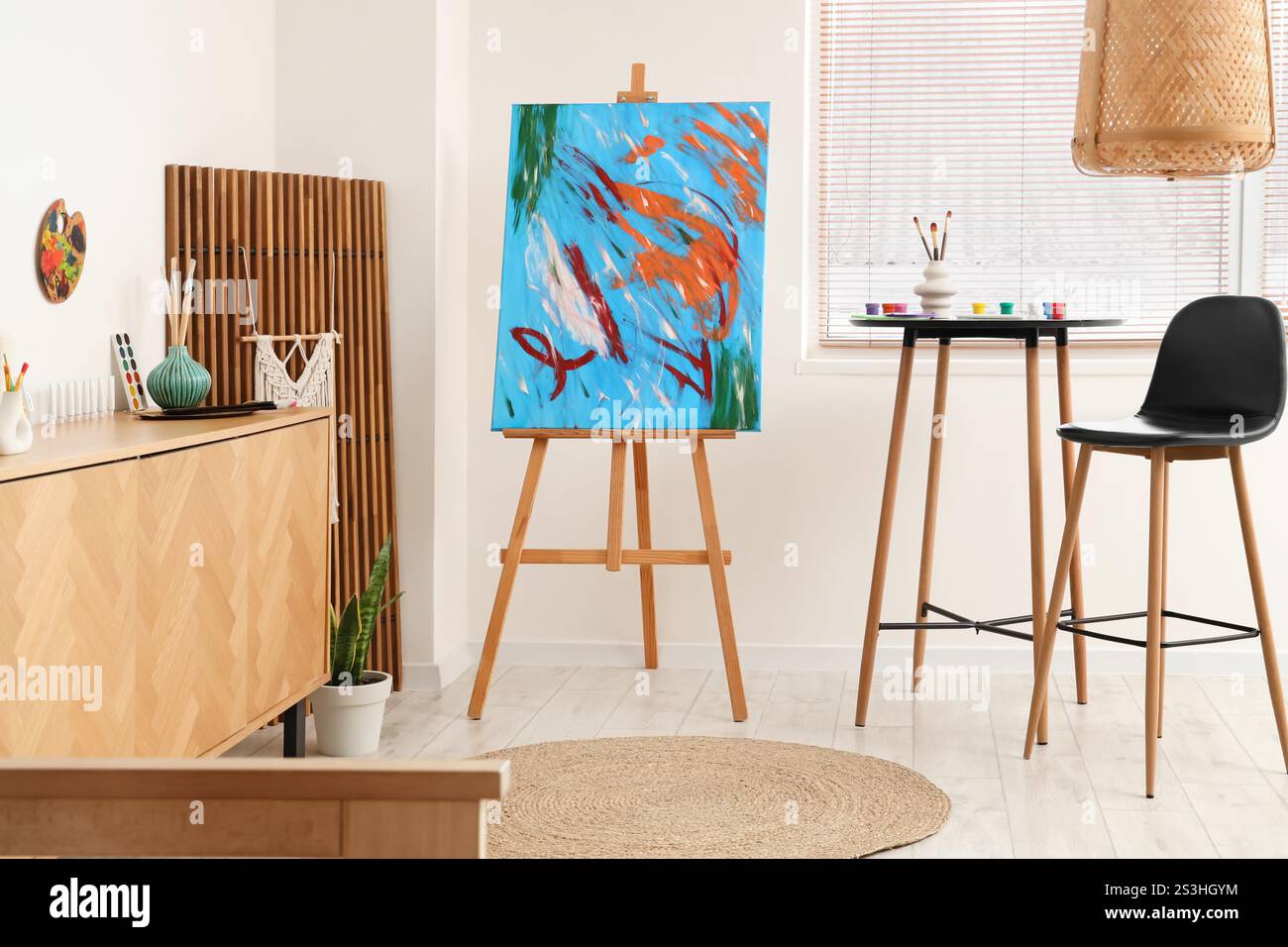 Picture on easel, chest of drawers and table with chair in painter's ...