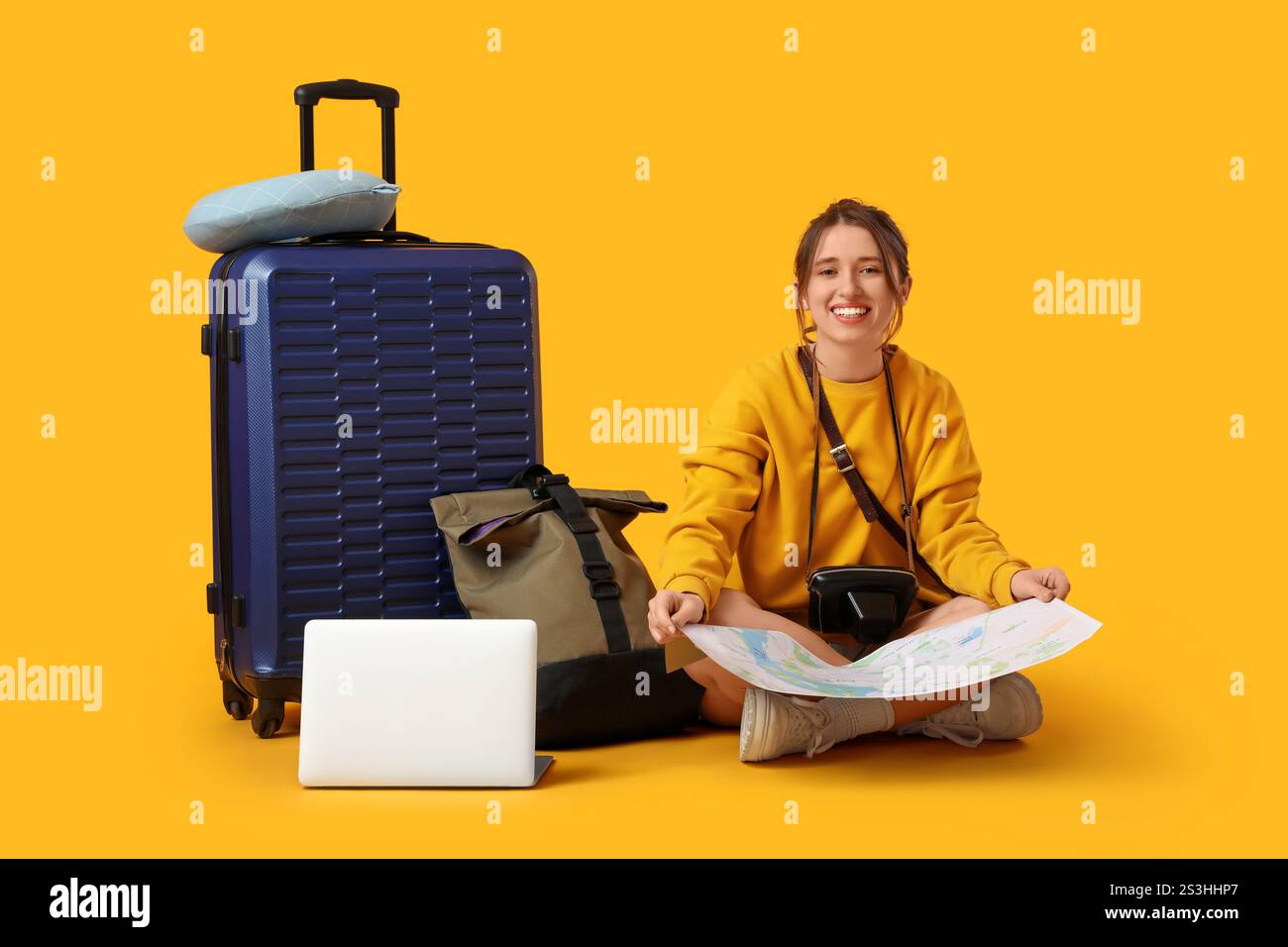 Female traveler with map and bags sitting on yellow background ...