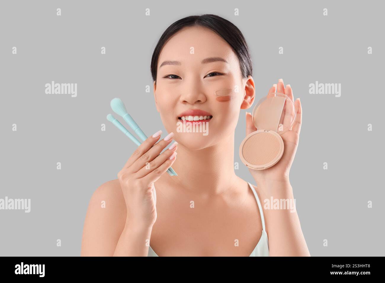 Beautiful Asian woman with powder, tonal foundation and makeup brushes ...