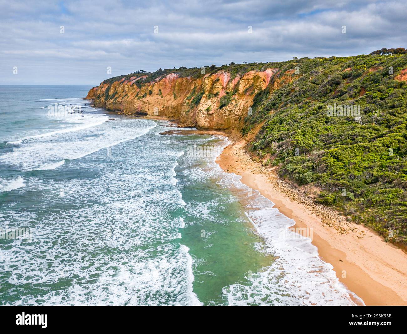 Aerial view of waves on a narrow beach below rugged cliffs at Aireys ...