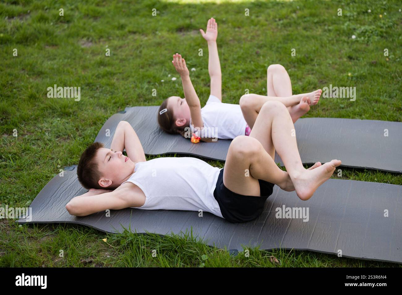 Two children, a boy and a girl, perform stretching exercises on gray ...