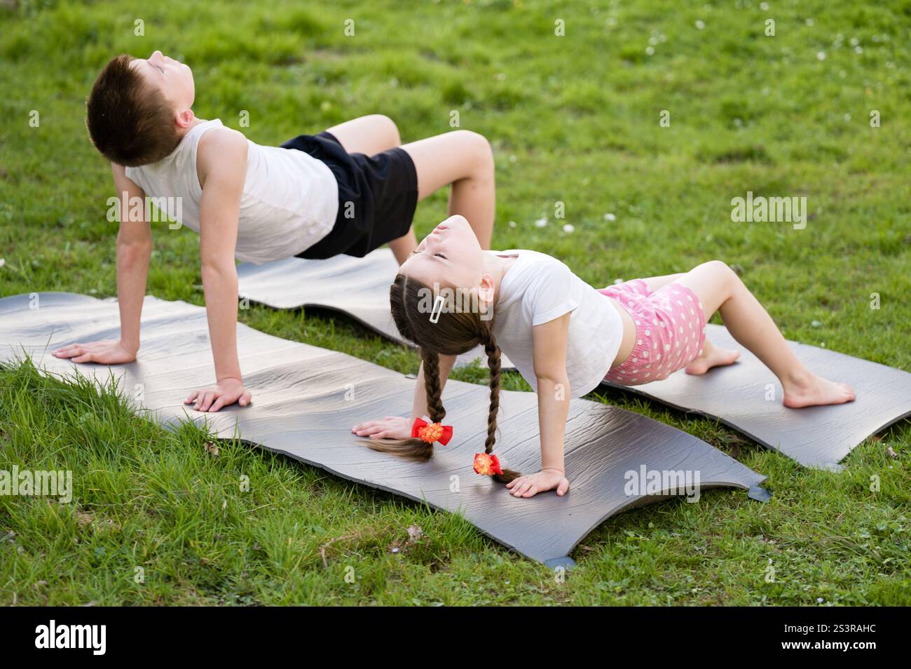 Two children, a boy and a girl, perform yoga poses on exercise mats in ...