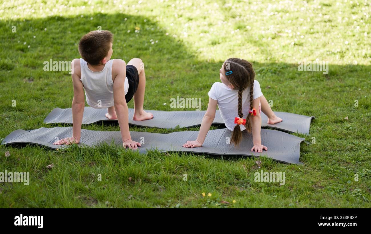 Two children, a boy and a girl, perform yoga poses on exercise mats in ...