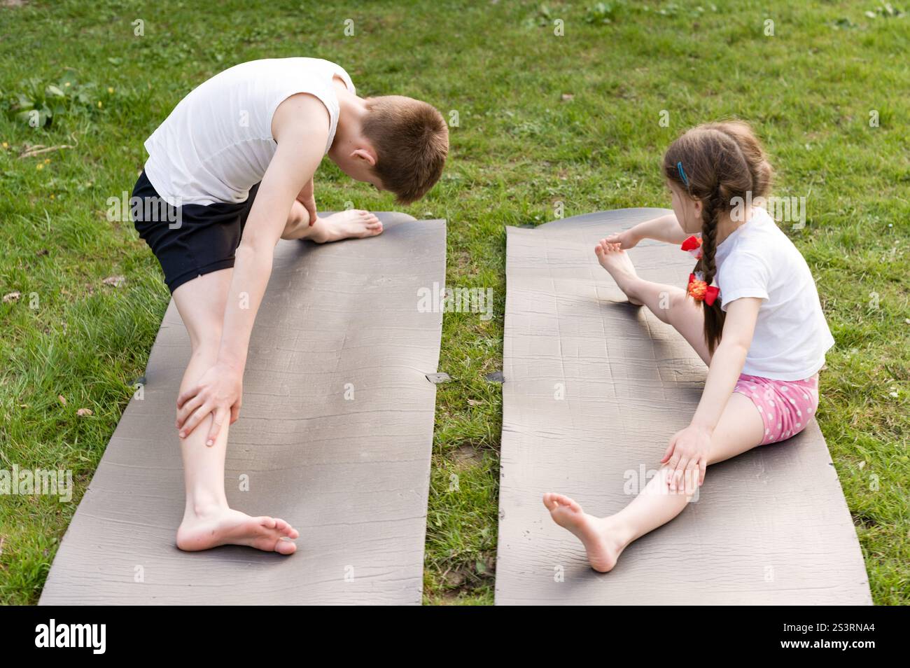 Two children, a boy and a girl, perform stretches on individual yoga ...