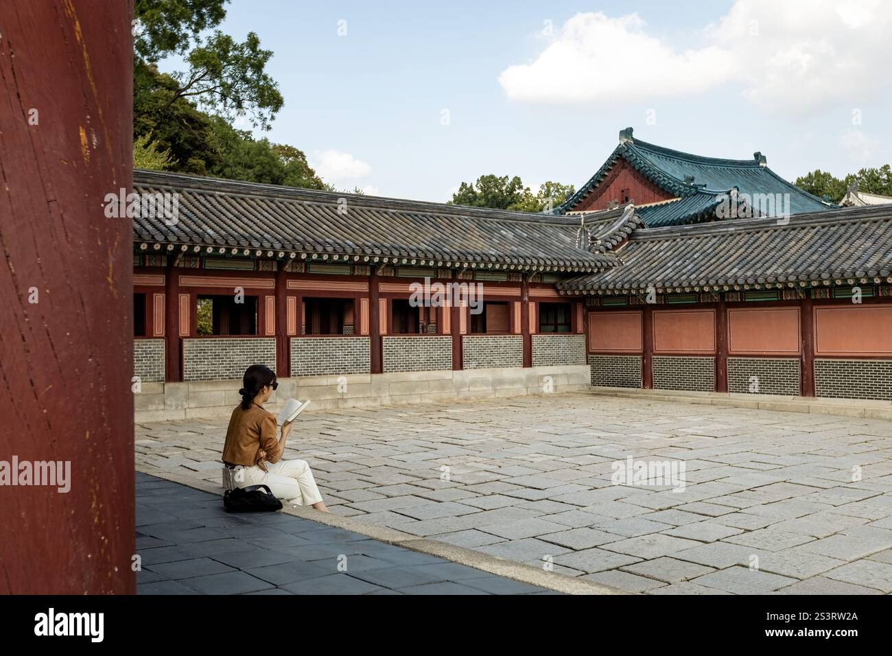 Korean girl reading book seated with traditional Korean temple ...