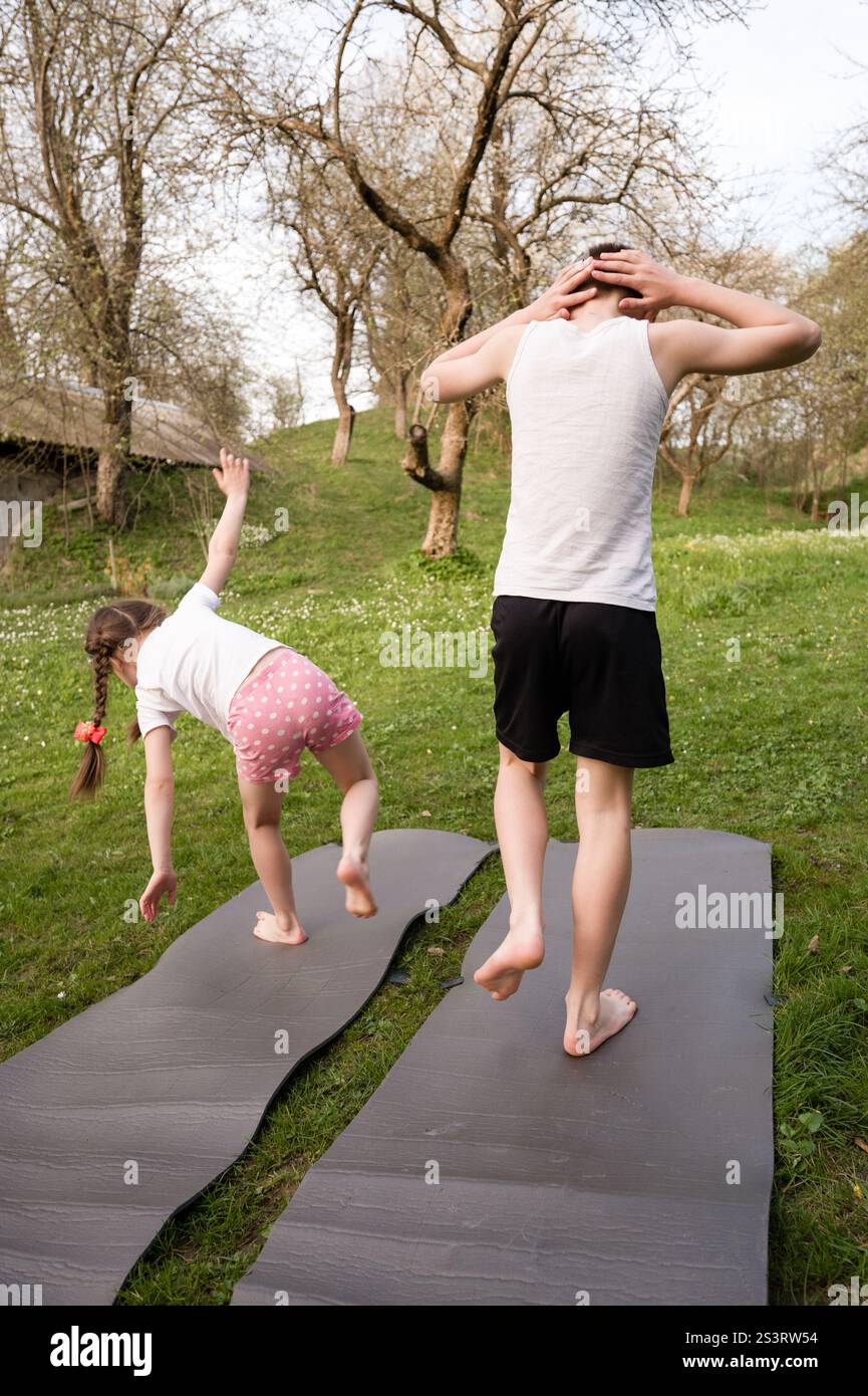 Two siblings, a boy and a girl, perform stretches and yoga poses on ...