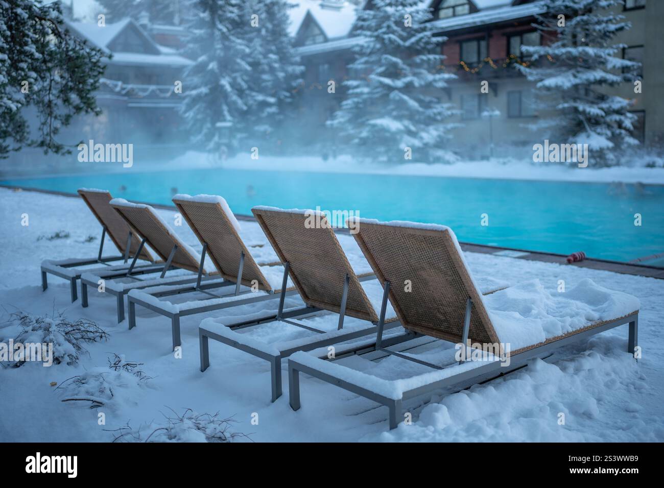 Warm open-air swimming pool with blue water and snow covered loungers ...