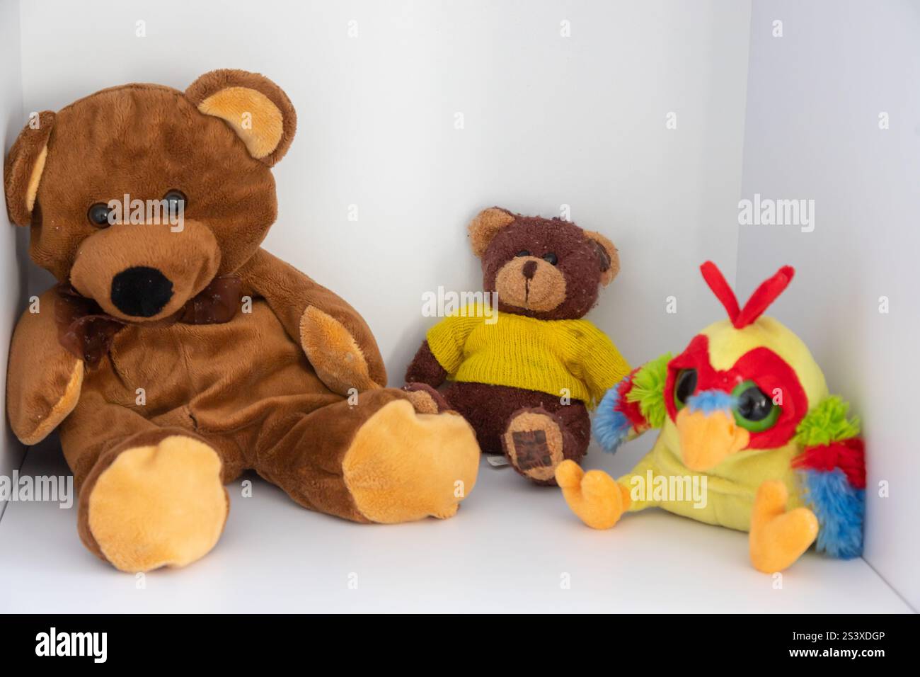A collection of three soft toys sits together on a white shelf. The ...