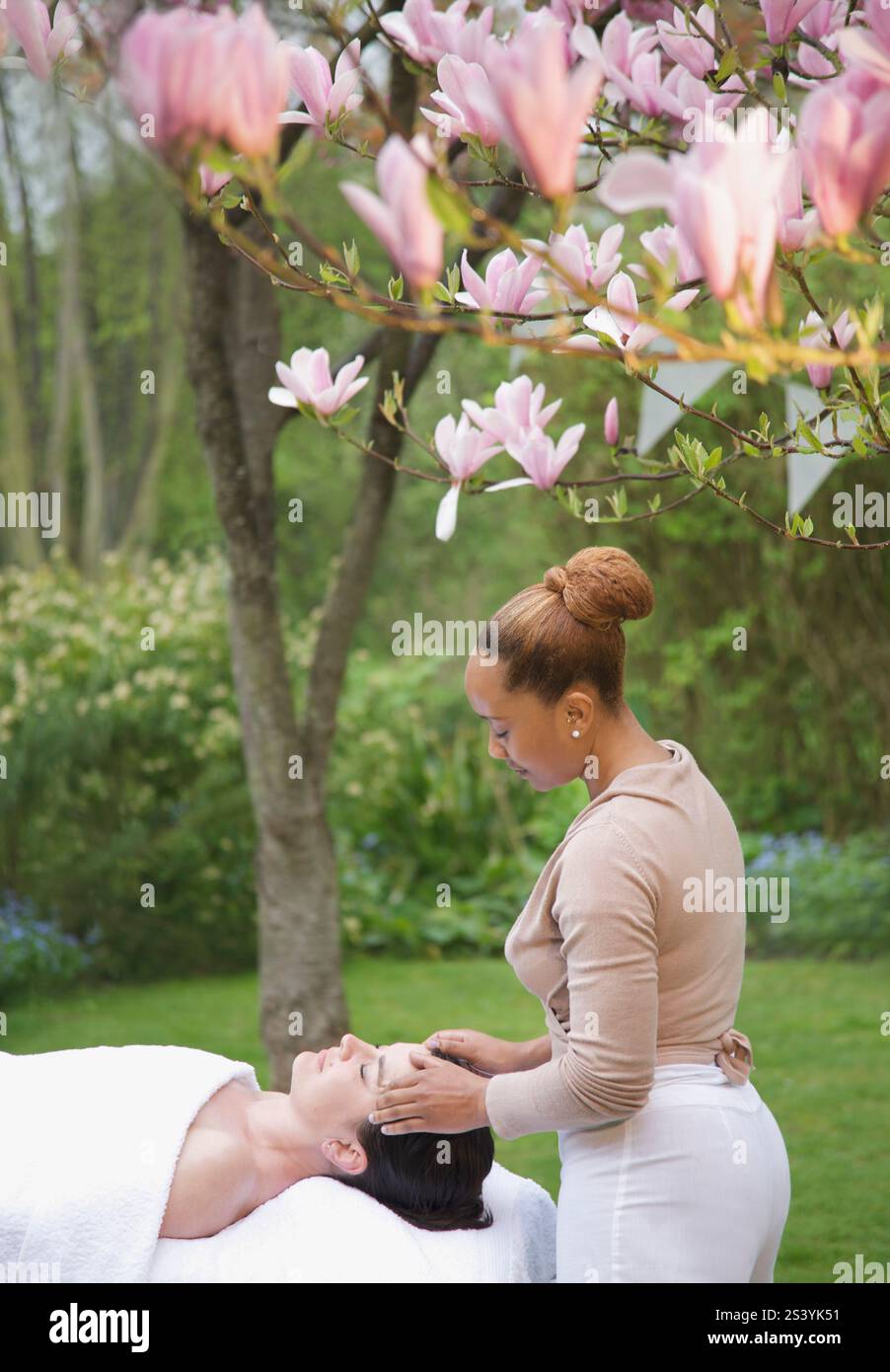 Masseuse giving a woman a facial massage under a magnolia tree Stock ...