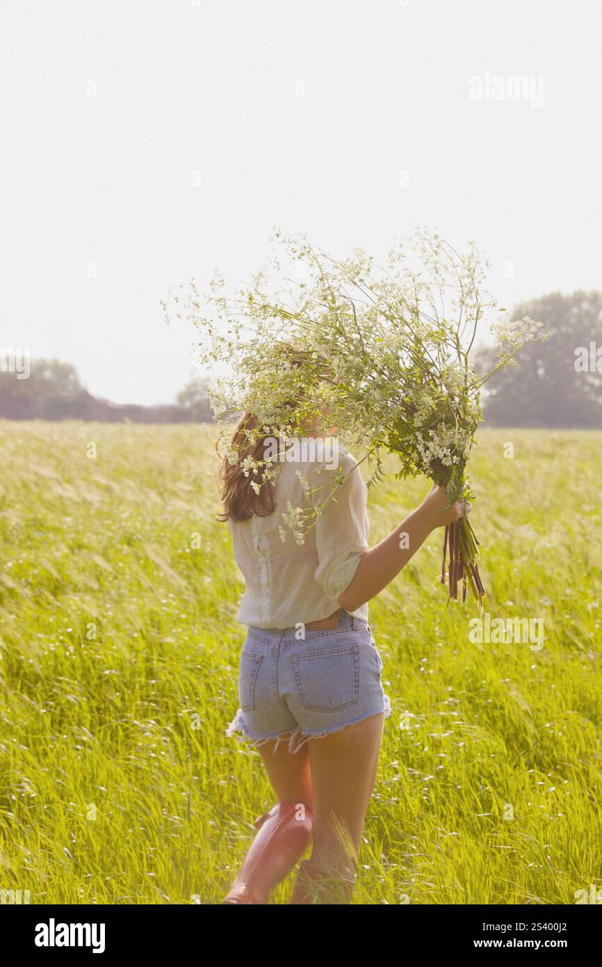 Back View of Young Woman in a Field Holding a Bunch of Wildflowers ...