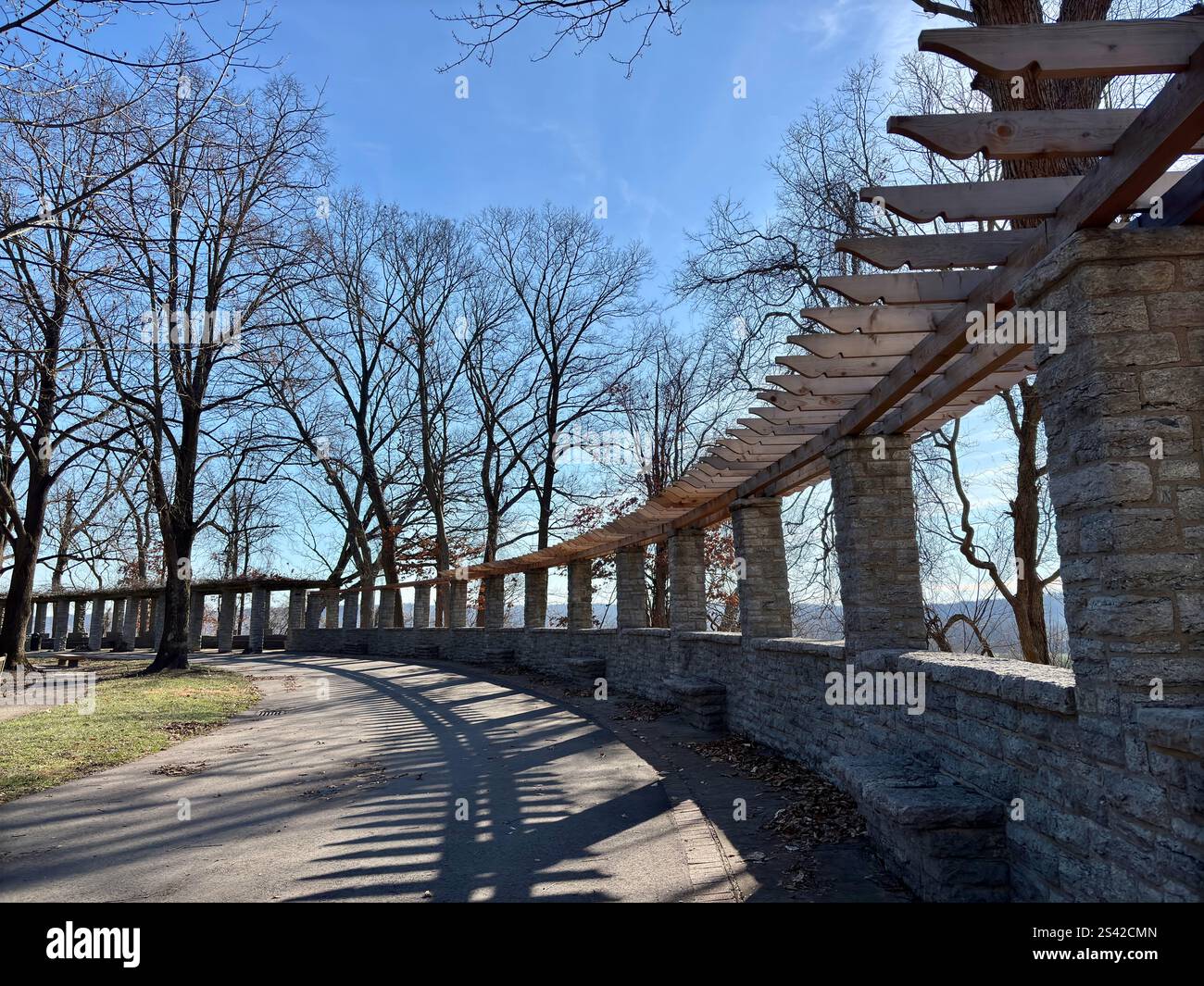 Stone pergola with wooden beams casting shadows on a curved pathway ...