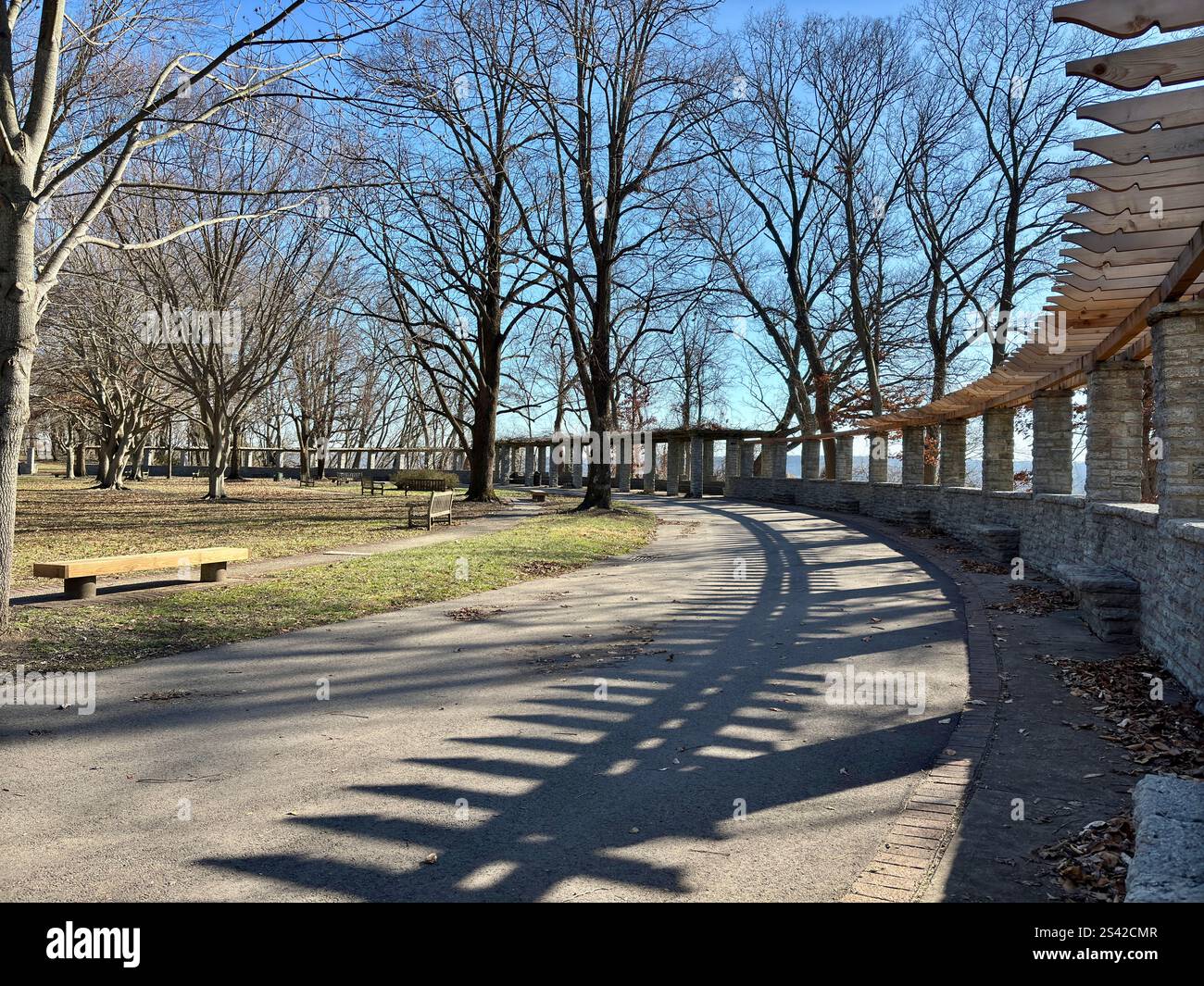 Curved pathway with benches and a stone pergola in a tree-lined park ...