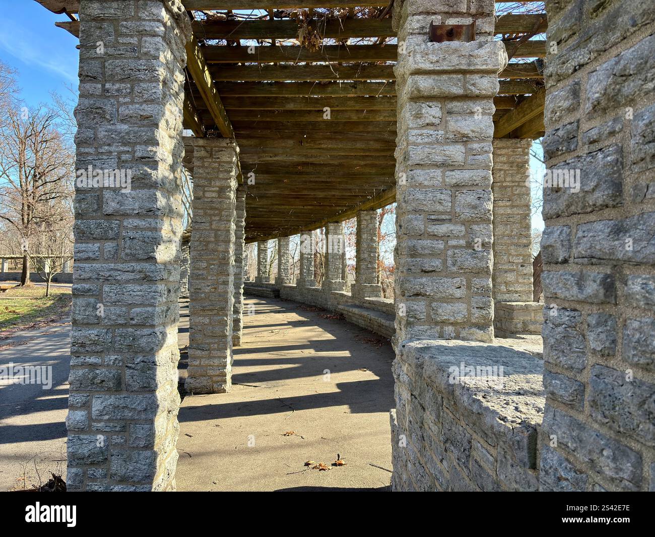 Stone pergola with wooden beams and textured columns casting shadows ...