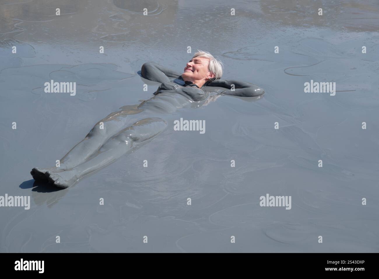 Senior woman with short gray hair relaxing in natural mud bath, fully ...