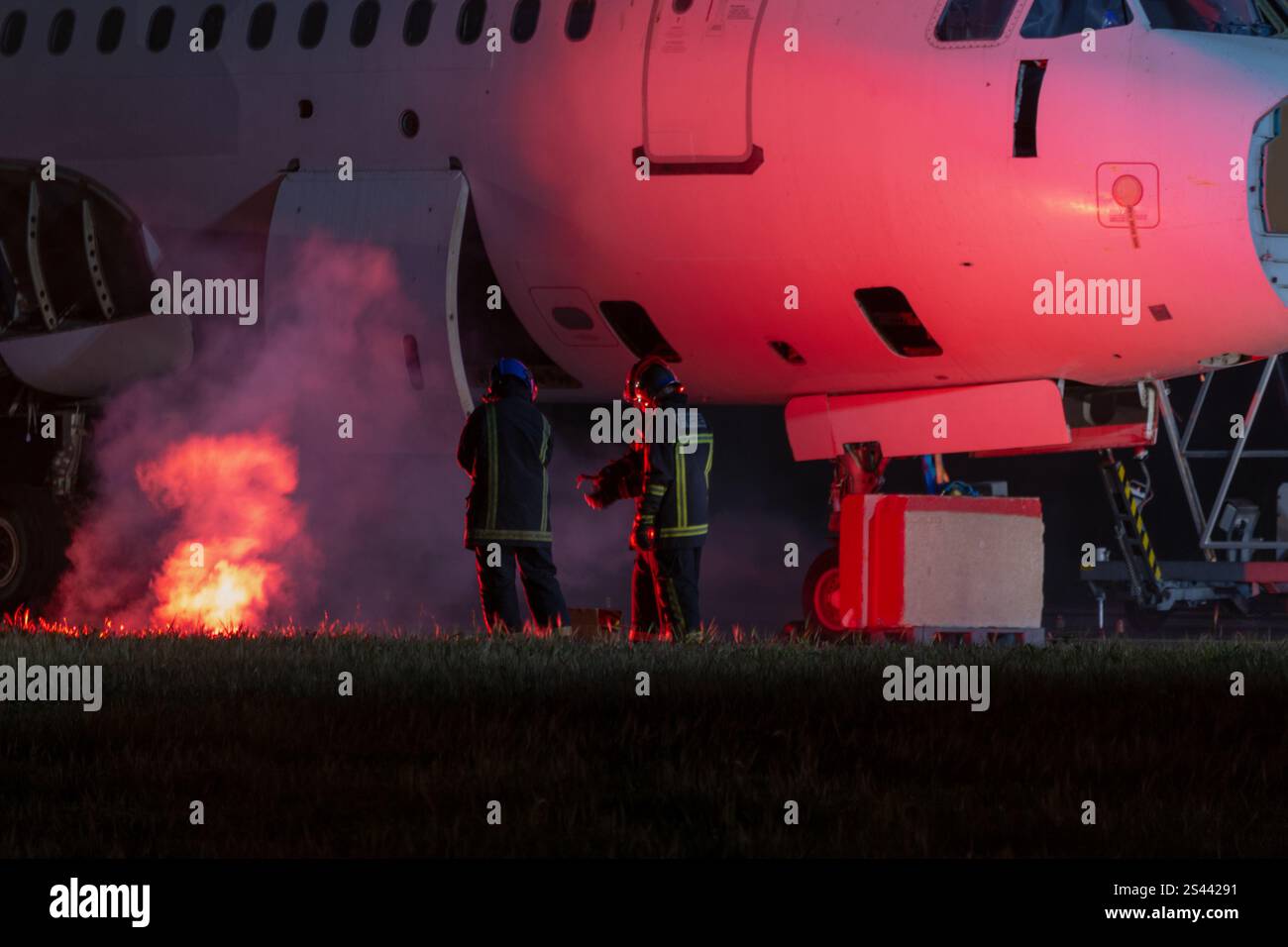 Two fire department officers beneath an air plane in the glowing light ...