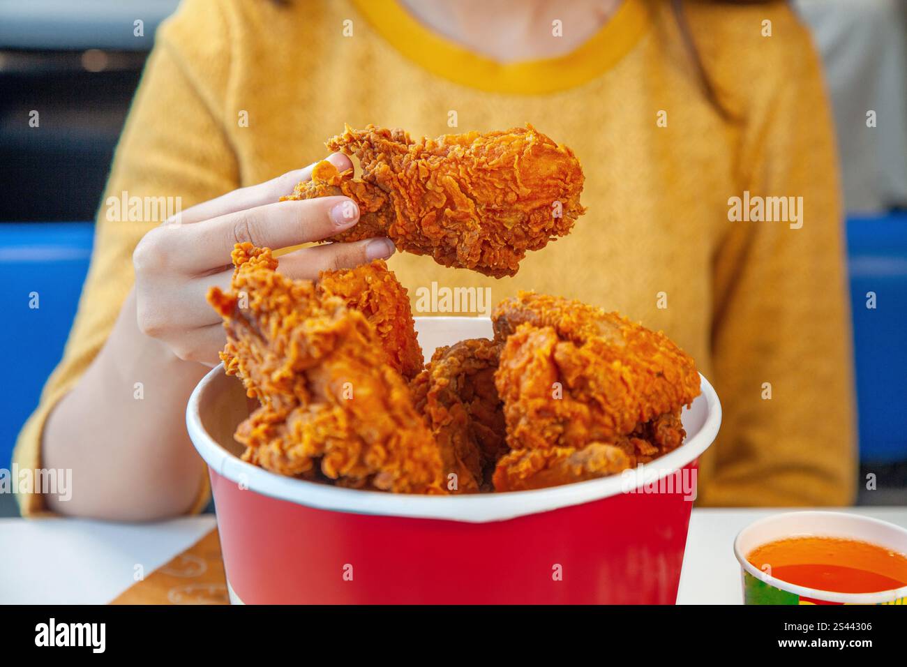 Girl holding a fried chicken drum stick with a bucket full of chicken ...