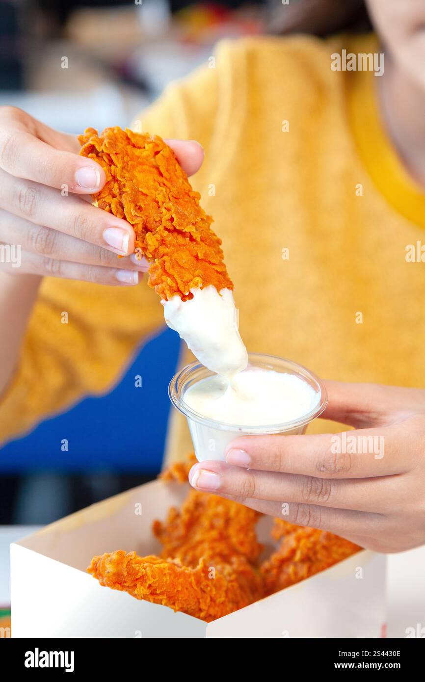 Girl holding fried chicken strip dunking in spicy mayo sauce with more ...
