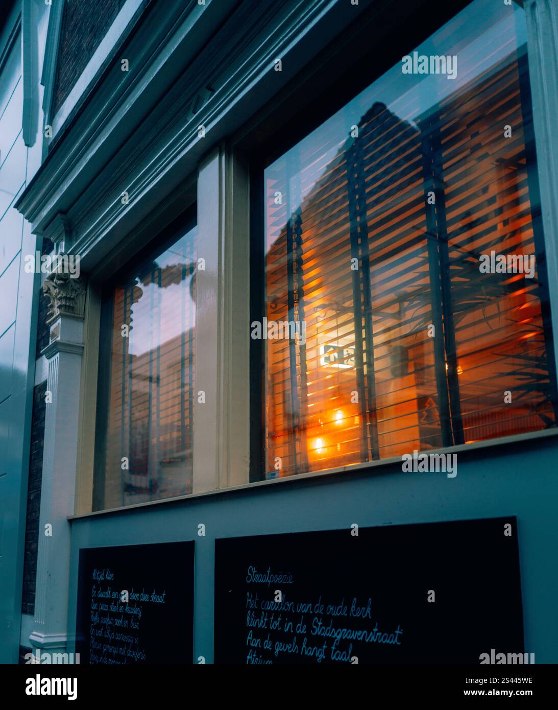 Close-up of a reflective glass window with blinds and warm light ...