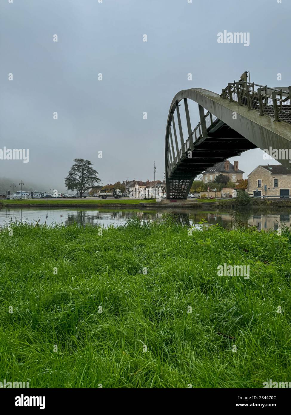 A curved bridge spans over a tranquil river, surrounded by foggy hills ...