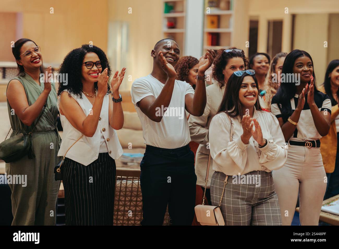 A diverse group of happy employees clapping and smiling in an office ...