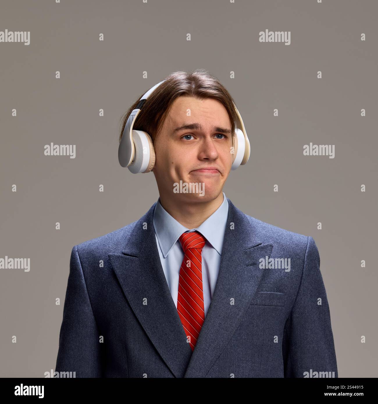 Portrait of man in suit with red tie wearing white headphones, looking ...