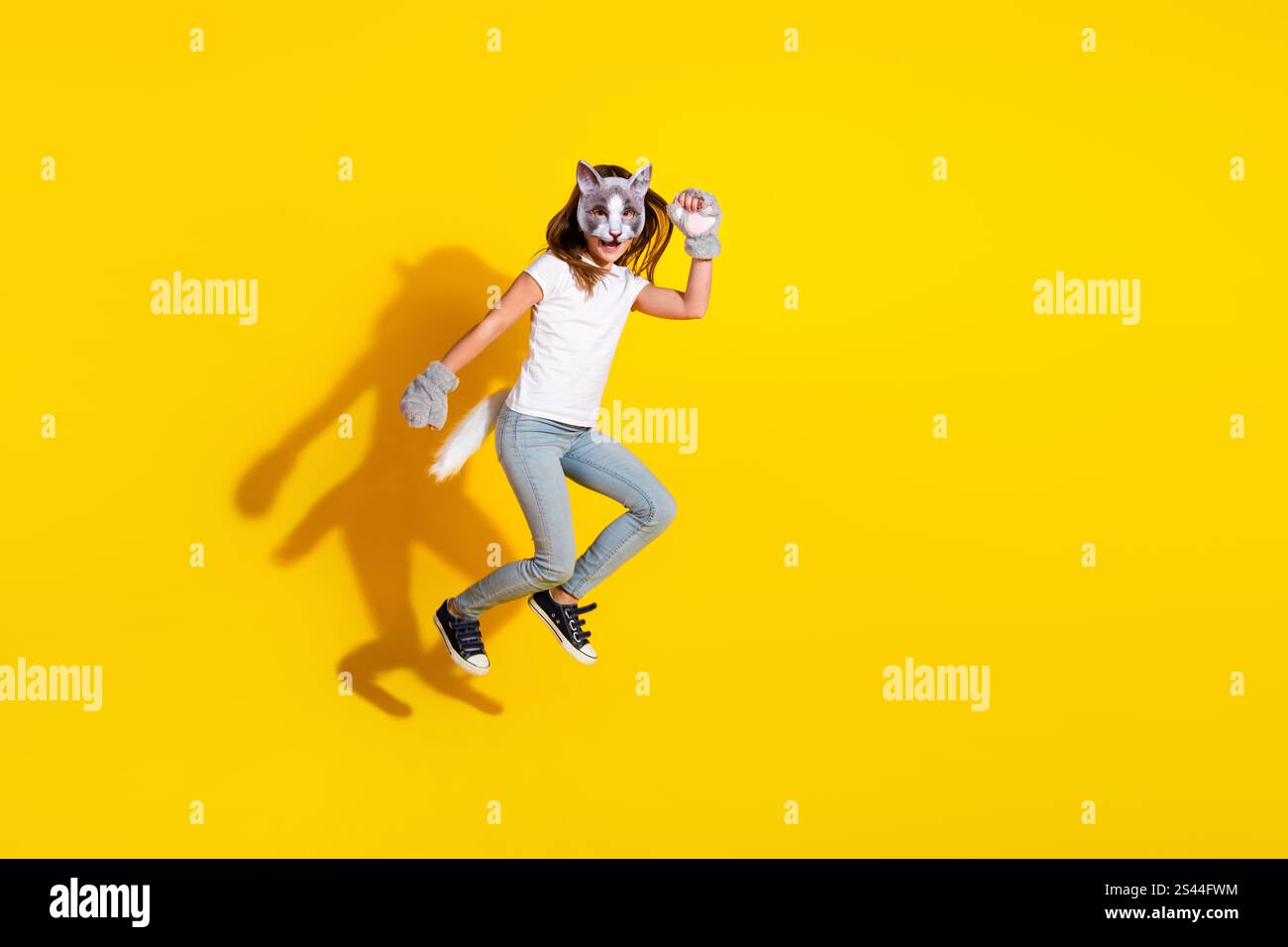Young girl jumping playfully in cat cosplay against a vibrant yellow ...