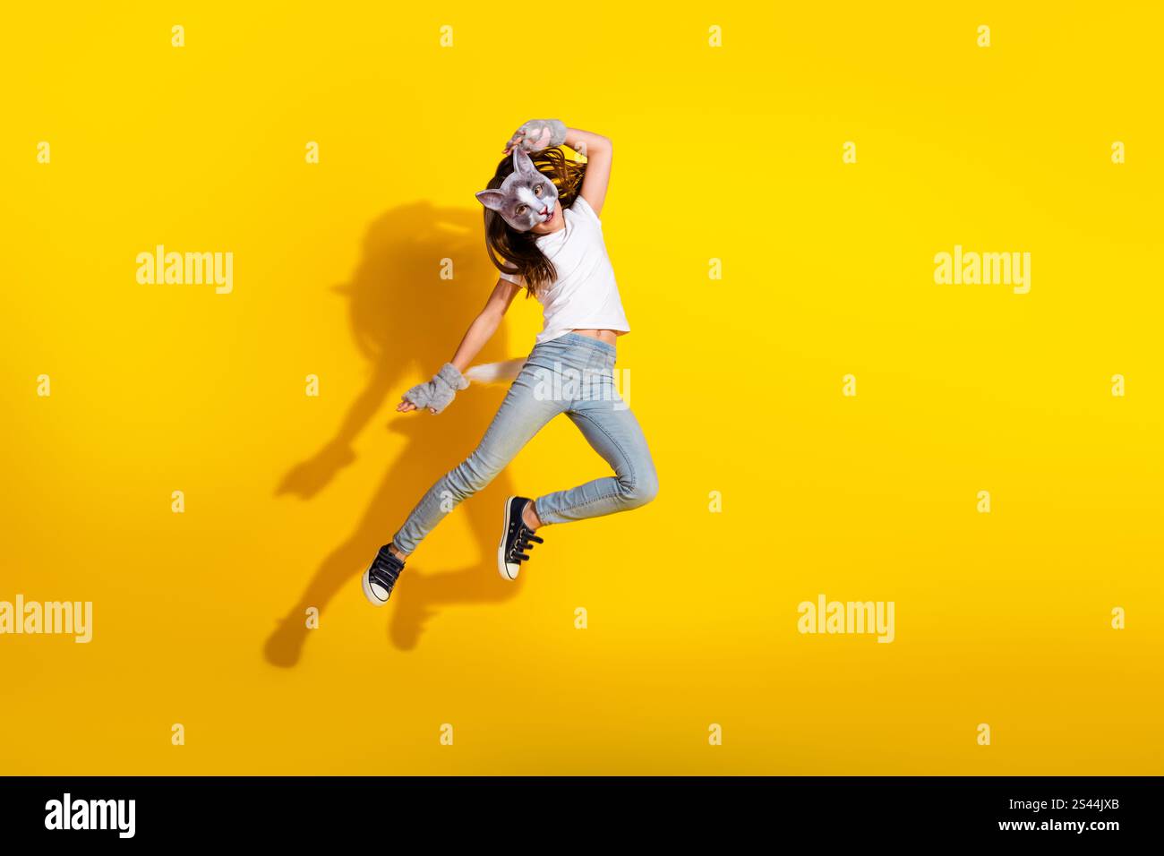 Young girl in casual outfit jumping with cat mask against yellow ...