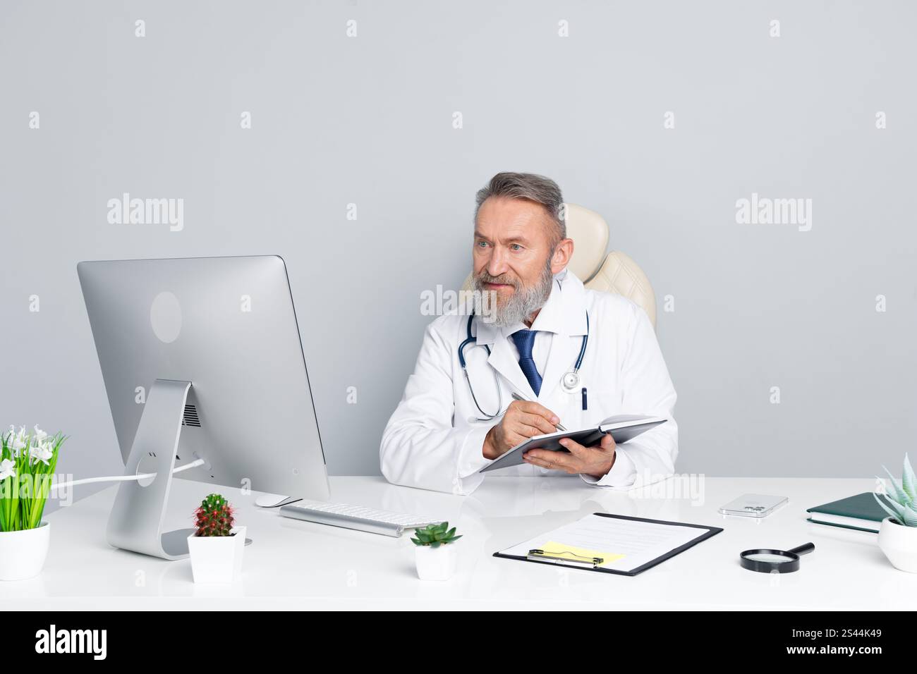 Senior doctor working at desk in white uniform with digital tools and ...