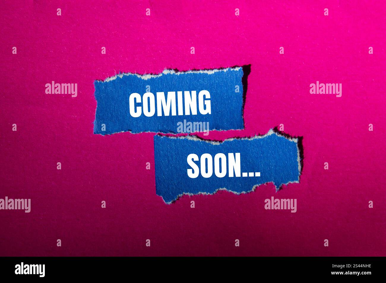 Coming soon message written on ripped torn blue paper pieces with pink ...