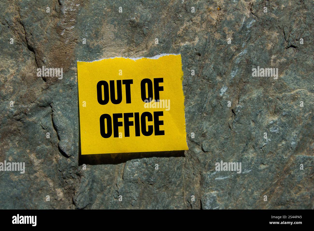 Out of office message written on ripped torn yellow paper piece with ...