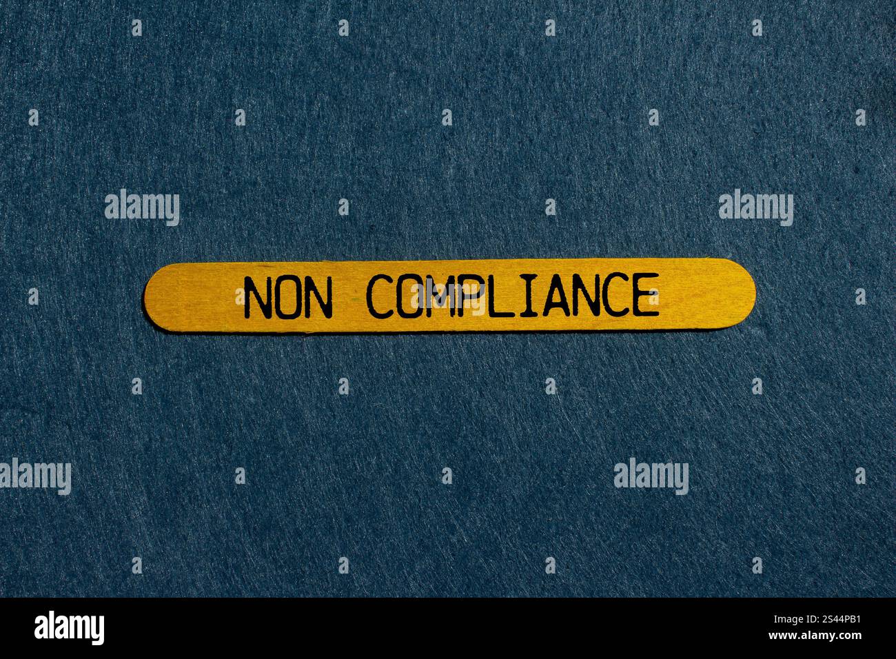 Non compliance message written on yellow wooden stick with gray background. Conceptual non ...