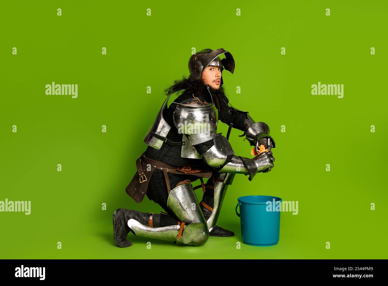 Young man in medieval knight armor kneeling with a cleaning bucket on a ...